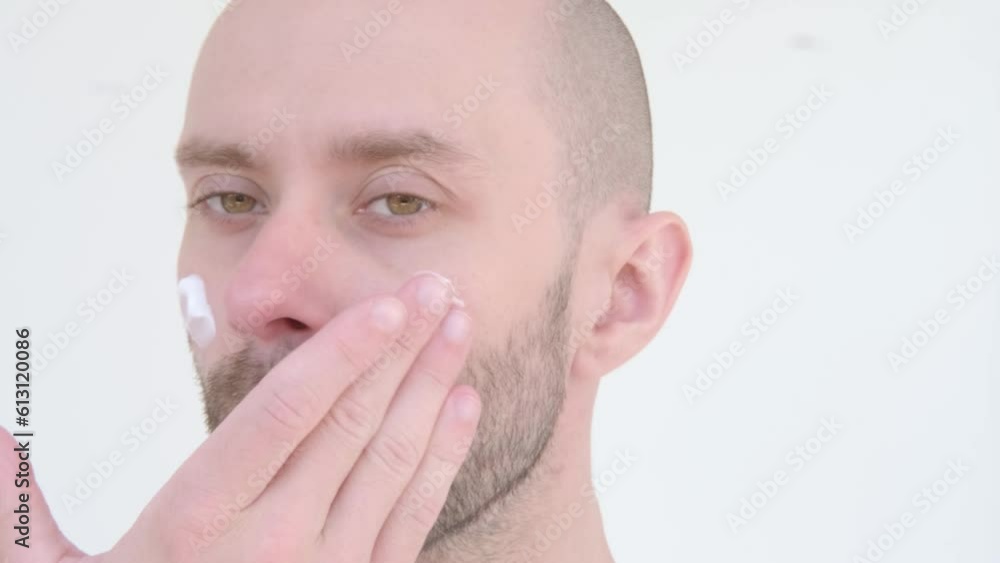 close-up of charismatic bearded young man 30 years old applies cream to ...