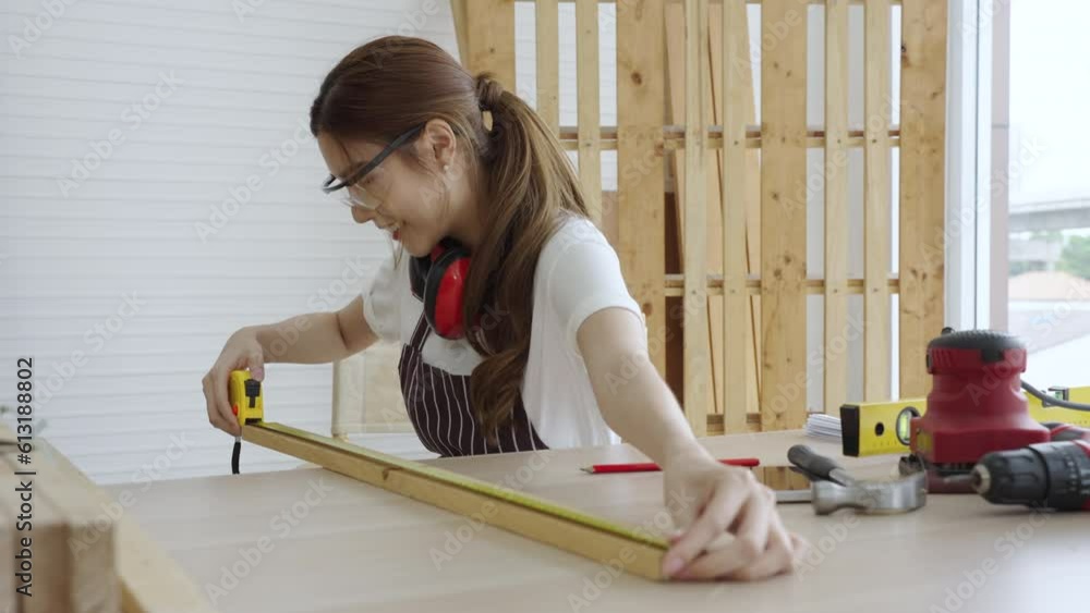 Beautiful Asian female carpenter using a tape measure to measure the ...