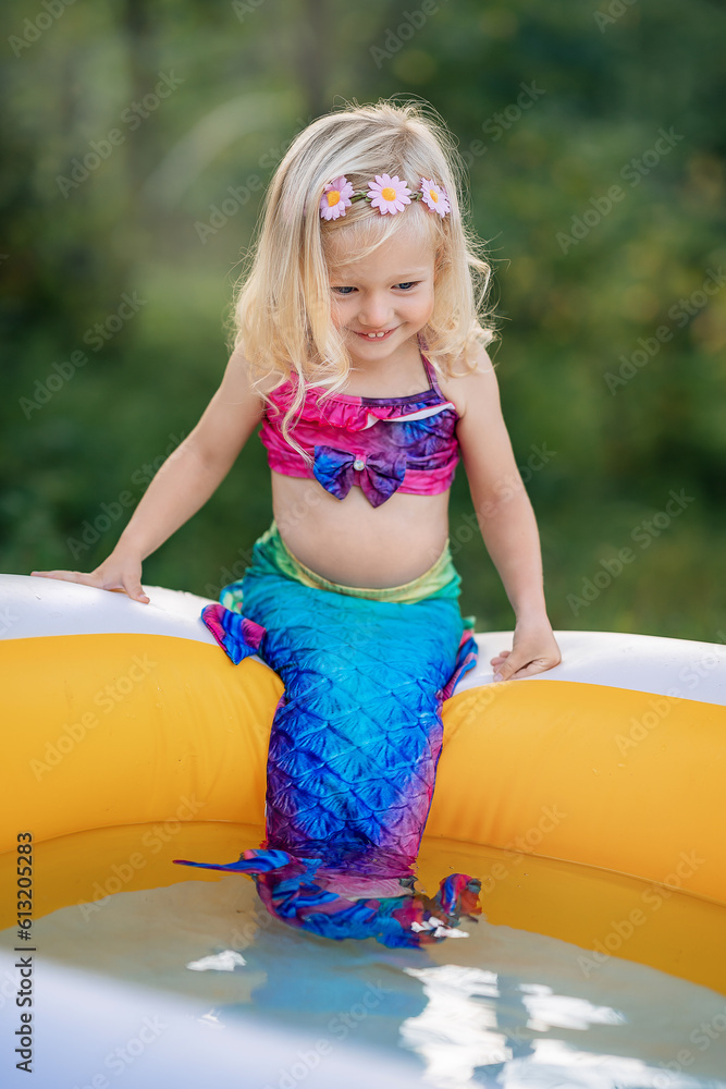 Little blonde toddler girl with mermaid bathing suit in splashing water ...