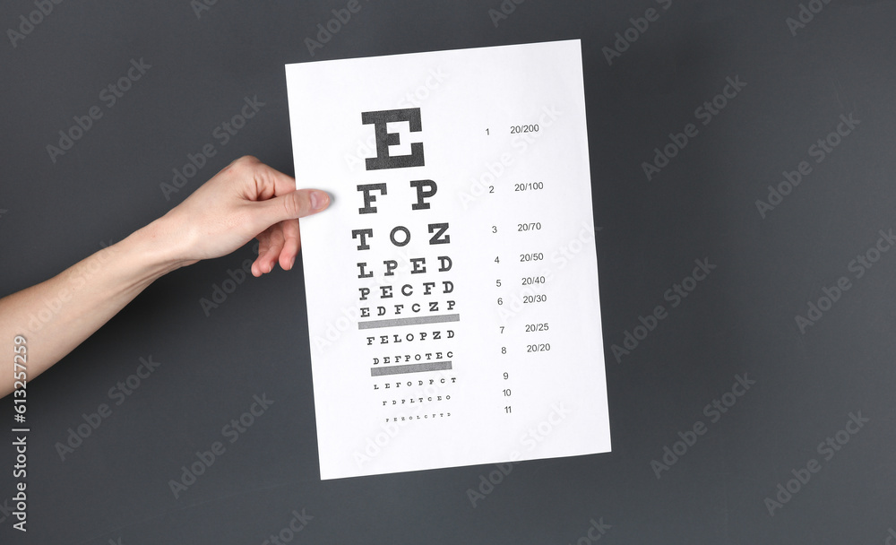 Hand holding eye test chart paper sheet on dark gray background. Vision ...