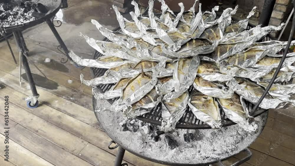 Many white fish cooked on round stand with fire in silver paper. Baked ...
