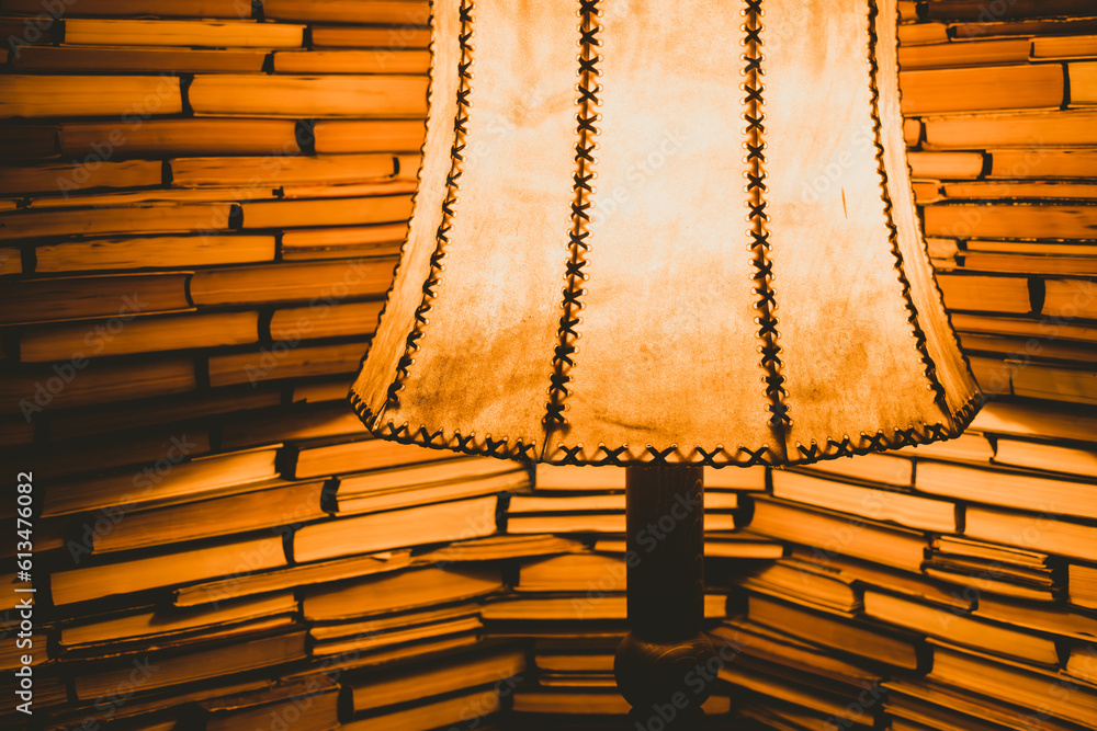 Old-fashioned lamp illuminating books stacked in the walls with warm ...
