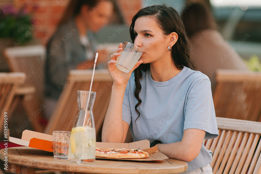 Young girl drinks lemonade and eats pizza in street cafe. Natural Stock ...