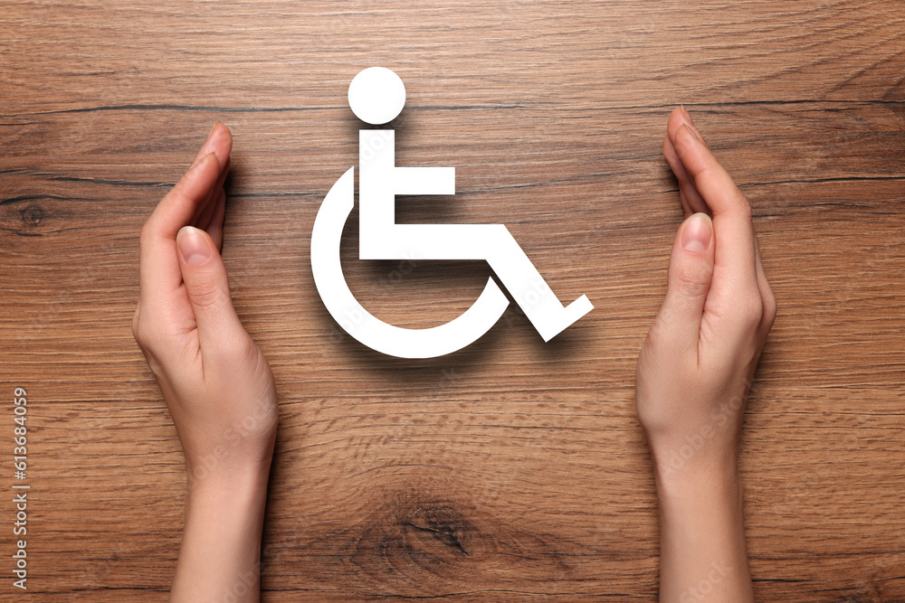 Disability inclusion. Woman protecting wheelchair symbol on wooden ...