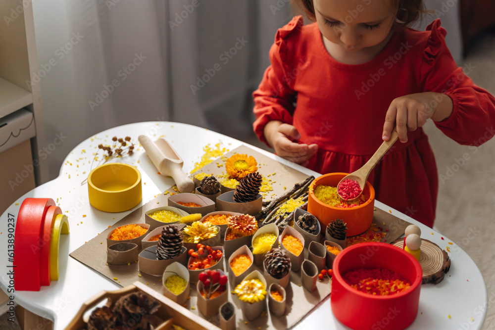 A little girl playing with autumn natural materials and make a tree ...