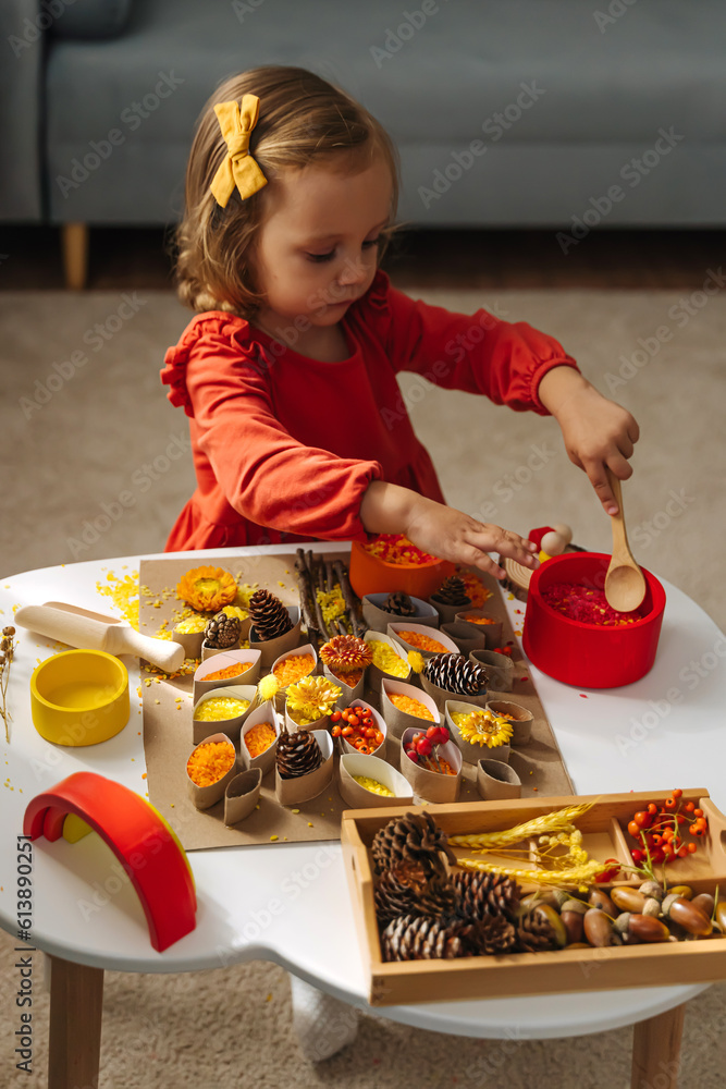 A little girl playing with autumn natural materials and make a tree ...