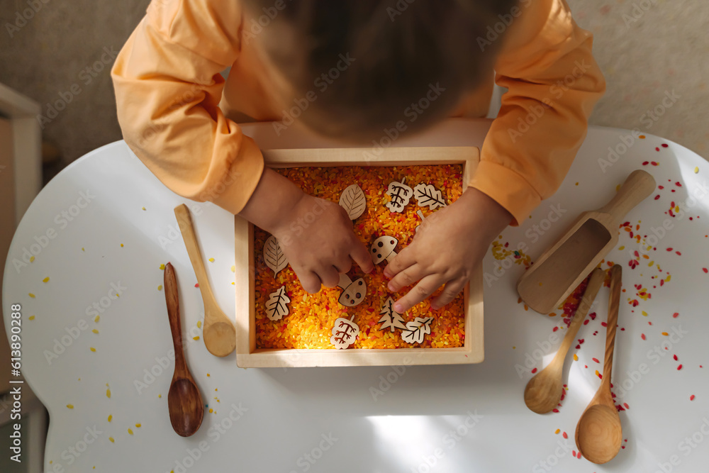 Foto de A little girl playing with colored rice in autumn sensory bin ...