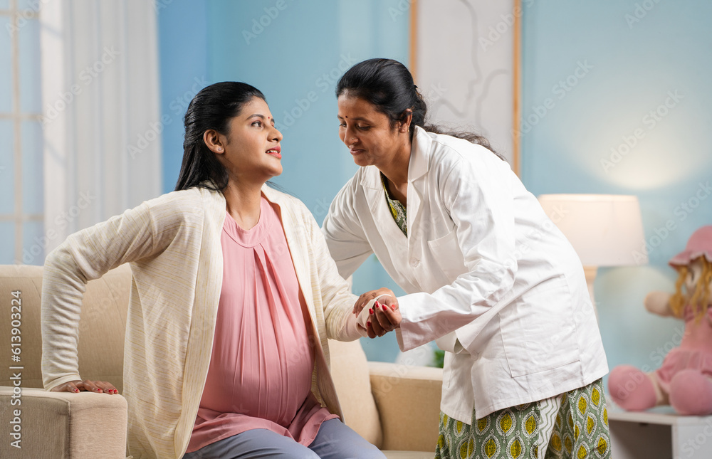 Indian nurse helping pregnant woman to get up from sofa at home ...