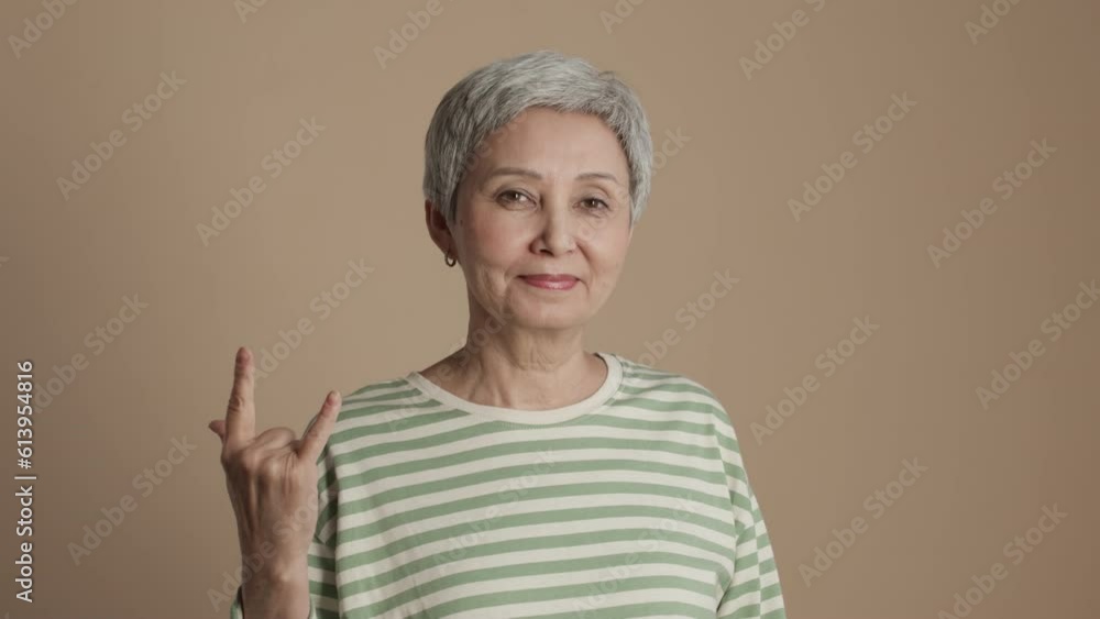 Medium portrait of grey haired Asian female boomer showing rock sign ...