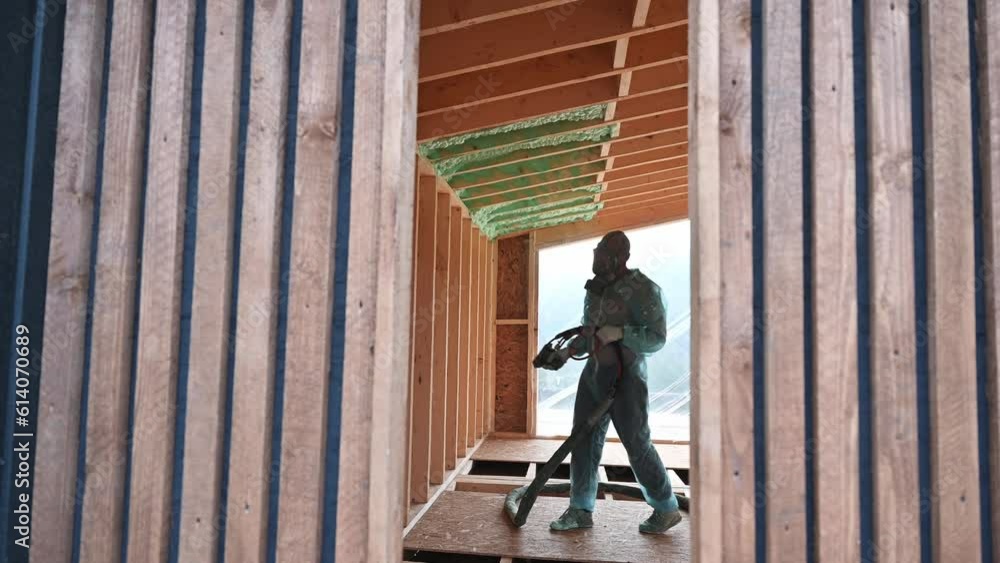 Male builder insulating wooden frame house. Man worker spraying ...