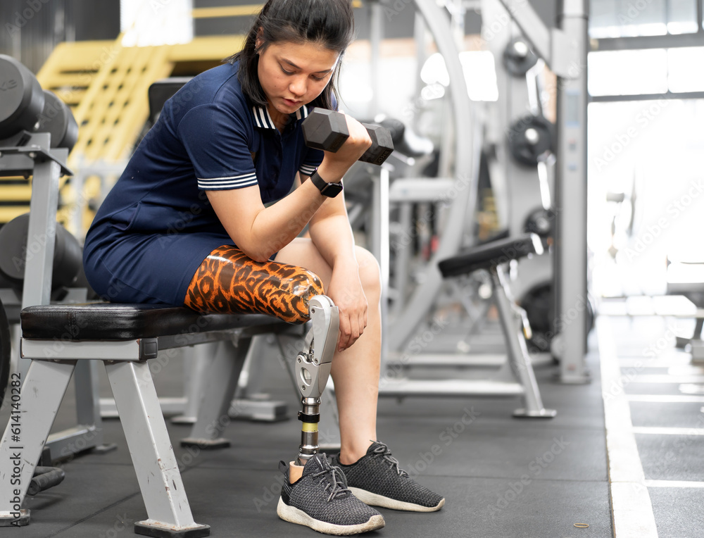 Woman with prosthetic leg sitting in gym lifting dumbbell weight. Asian ...