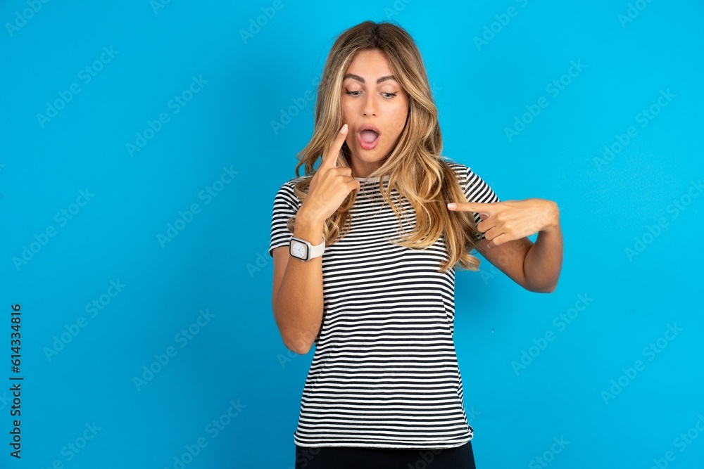 Shocked young beautiful woman wearing striped t-shirt look surprisedly ...