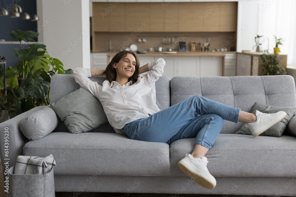 Cheerful millennial woman relax on sofa in studio apartment, leaned on ...