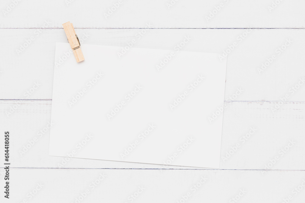 White paper card with wooden clamp on white table background for ...