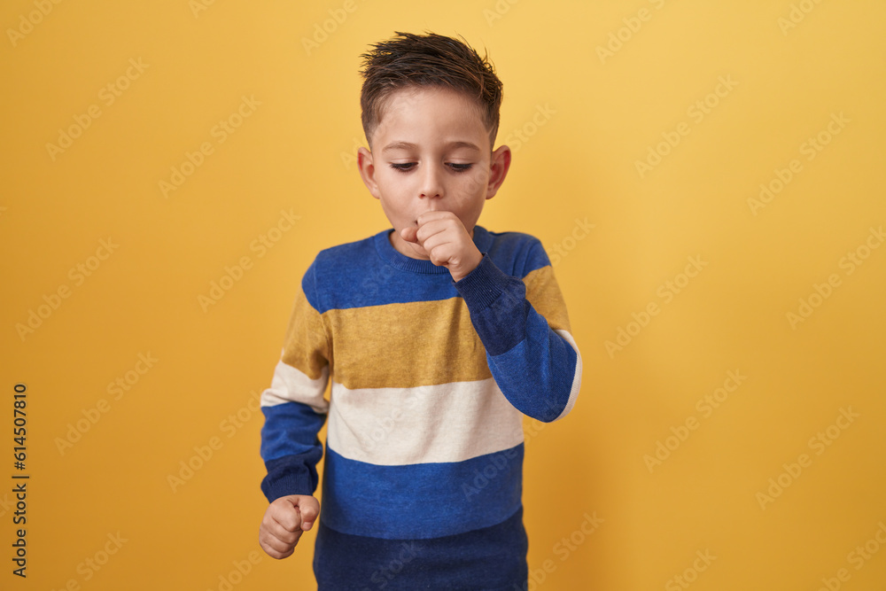 Little hispanic boy standing over yellow background feeling unwell and ...
