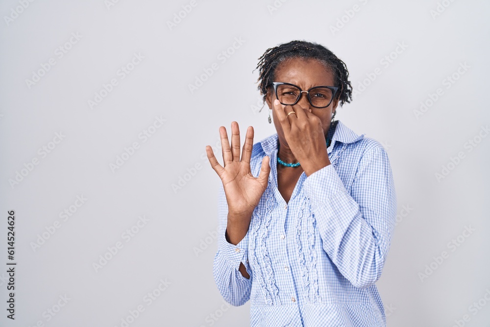 African woman with dreadlocks standing over white background wearing glasses smelling something ...