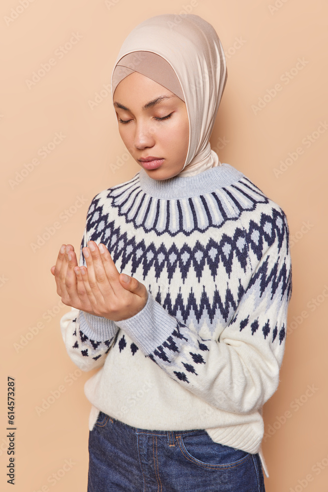 Calm young Muslim woman praying indoors wears headscarf and jumper ...