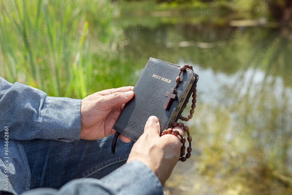 Christian man holding Holy Bible, religious cross and rosary beads by ...