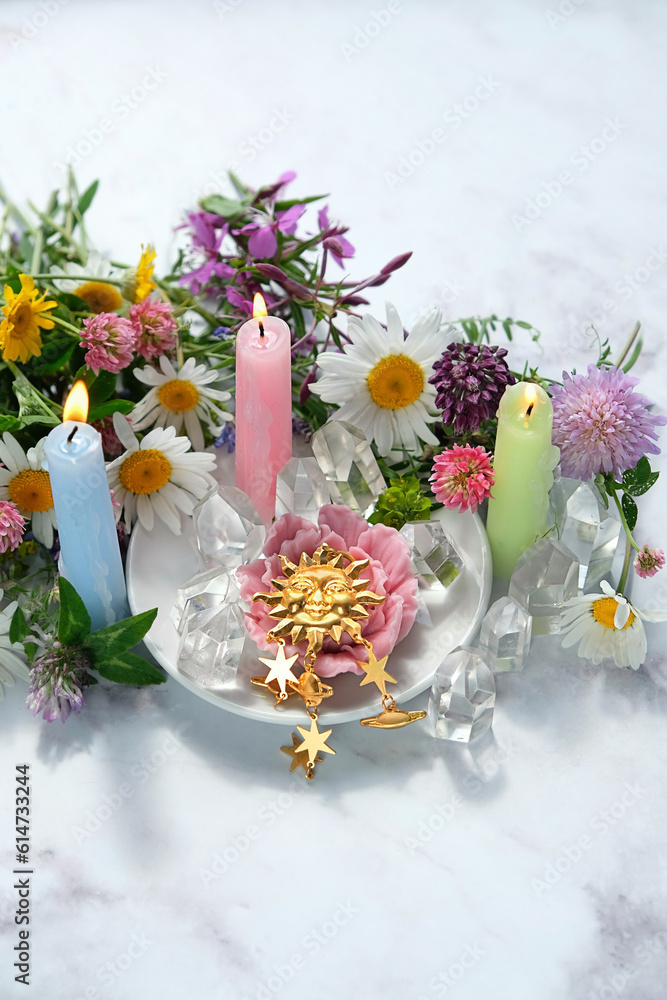 Burning candles, sun amulet, crystal gemstones and flowers on marble ...