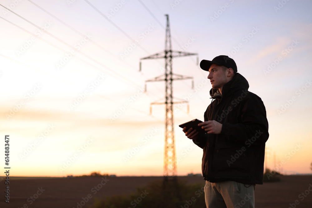 Young power engineer holds digital tablet against high voltage tower at ...