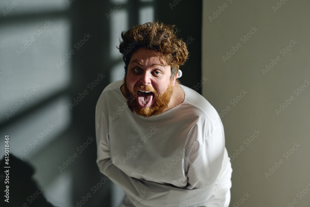 Young insane man in straitjacket showing tongue and screaming while ...