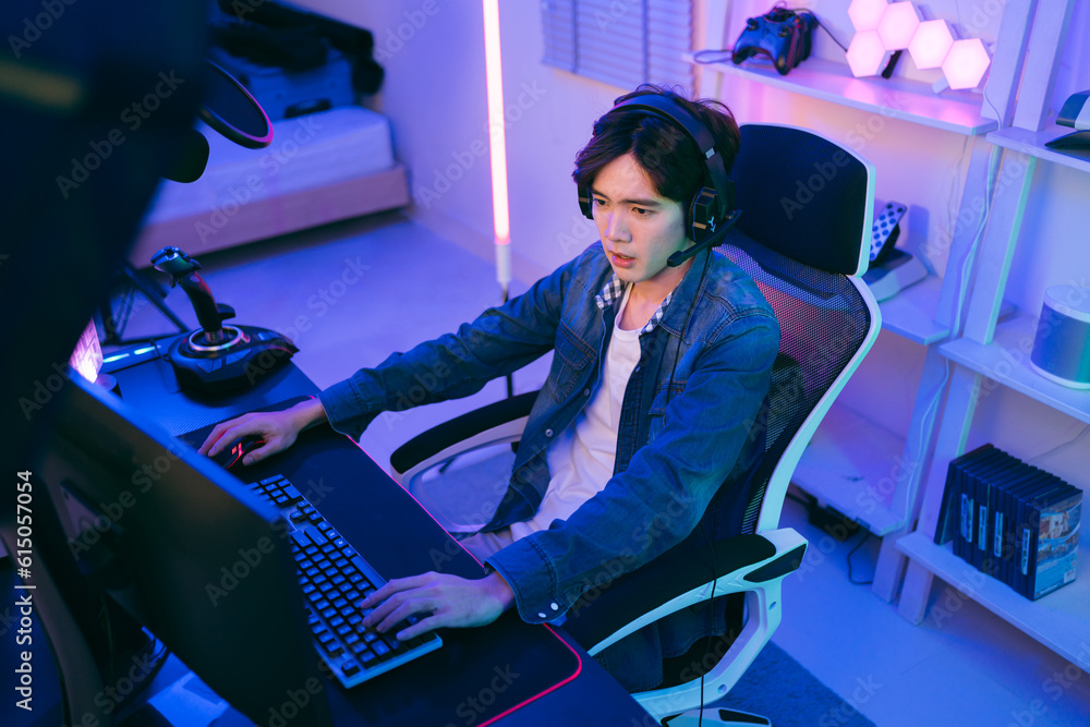 A young Asian man professional gamer wearing jeans jacket sits on a ...