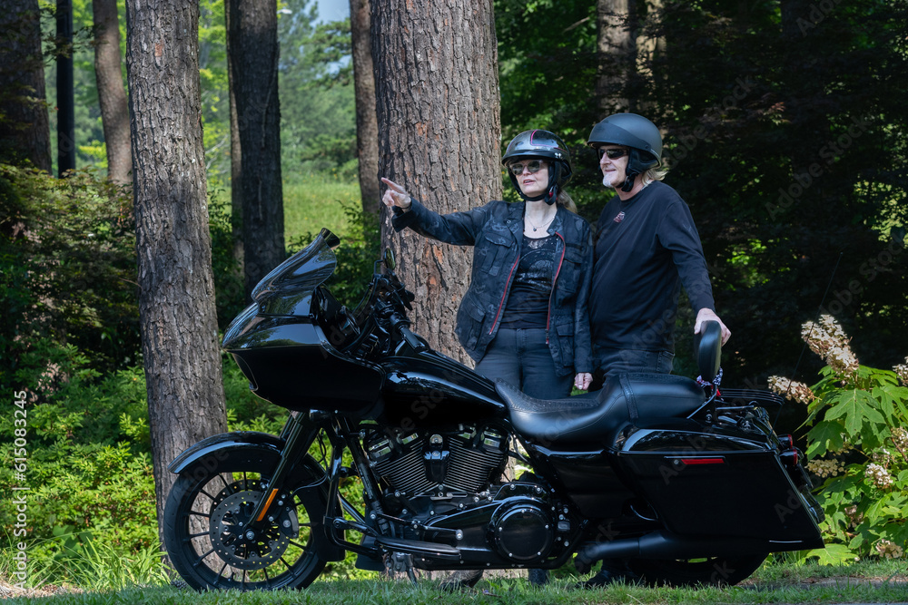 man and women motorcycle riders parked near mountain trees pointing at ...