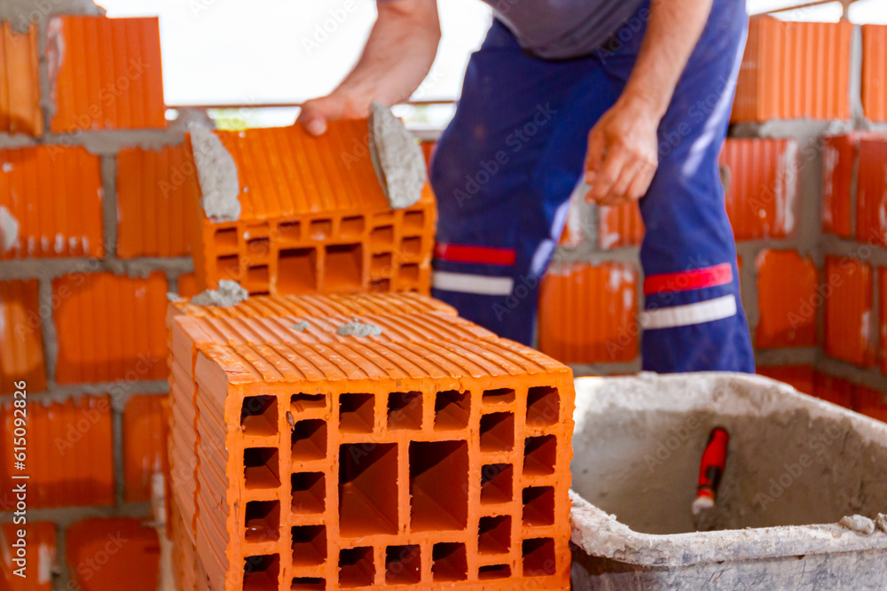 Close up shot on heap of red blocks, in background mason is building a ...
