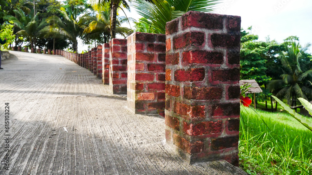 Red brick pillars line the hilly uphill road. Road with forest all ...