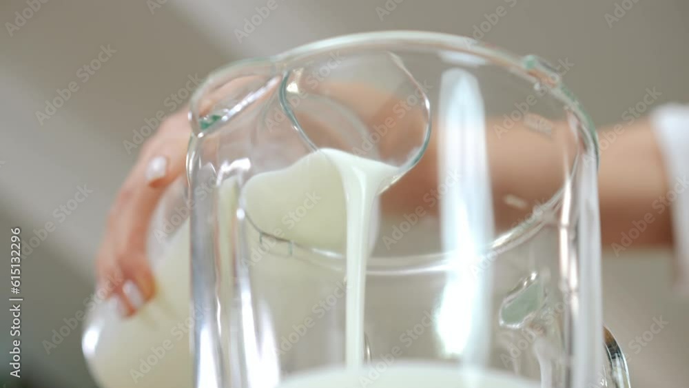 Closeup female hand pouring white milk in blender leaving in slow ...