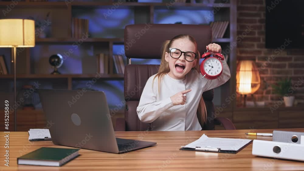 Positive little girl pulling out alarm clock from under table, pointing ...