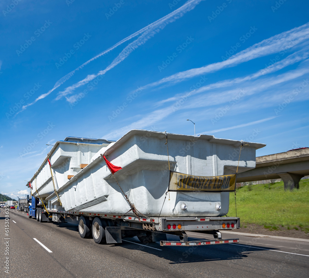 Blue big rig powerful semi truck transporting oversize cargo on flat ...