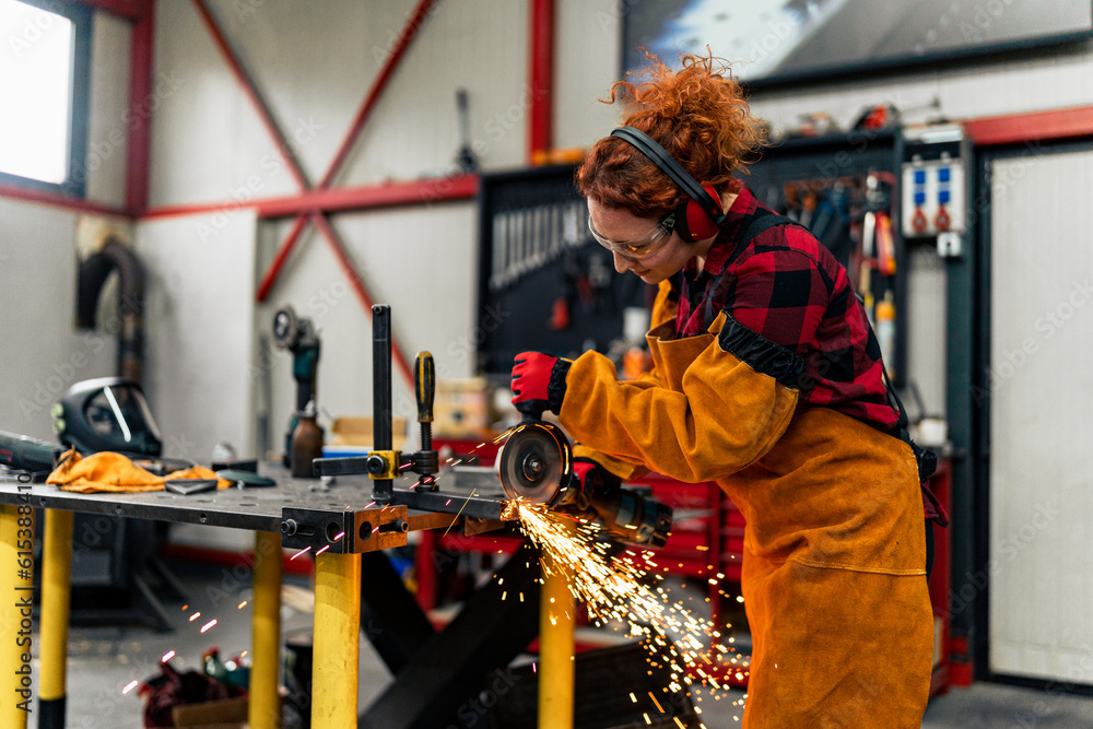 Woman in STEM using grinder to cut a metal bar, wearing gloves and a ...