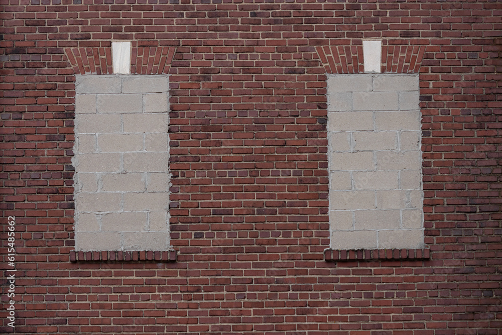 two windows sealed with cinderblocks on a red brick wall, with a ...