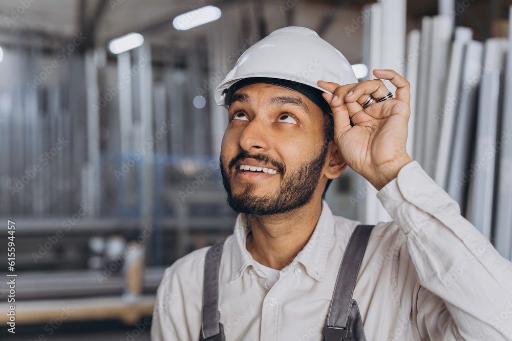 Portrait of a happy Hindu worker in a white hard hat and overalls ...