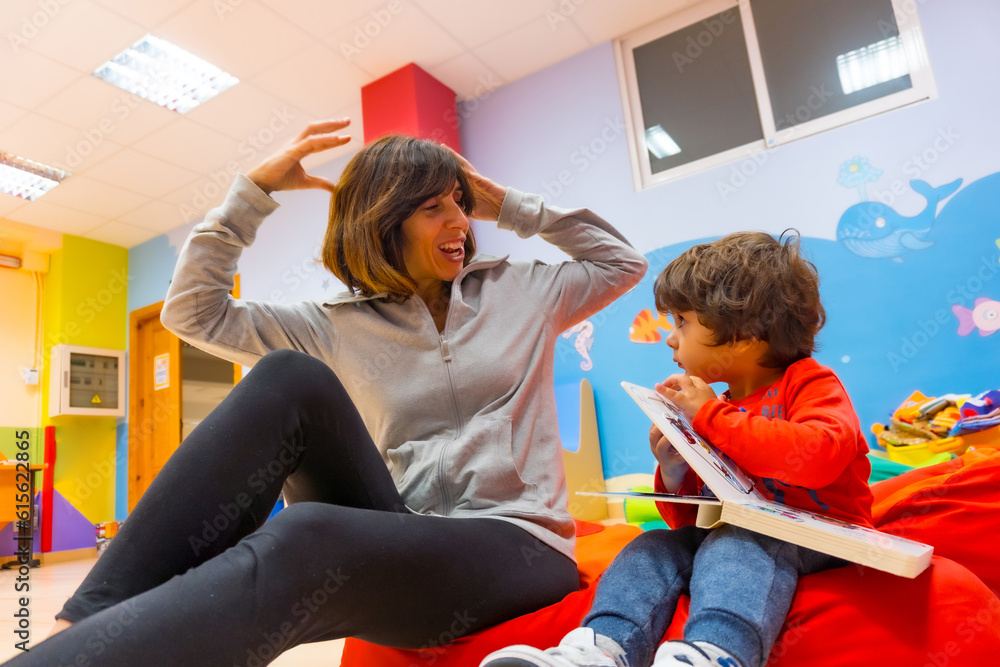 Woman teacher with a child sitting reading a book and expressing things ...