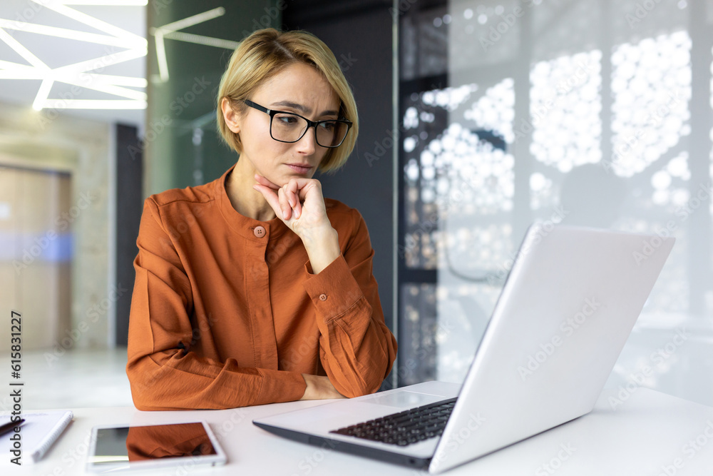 Serious thinking woman working with laptop inside office at workplace, businesswoman solving ...