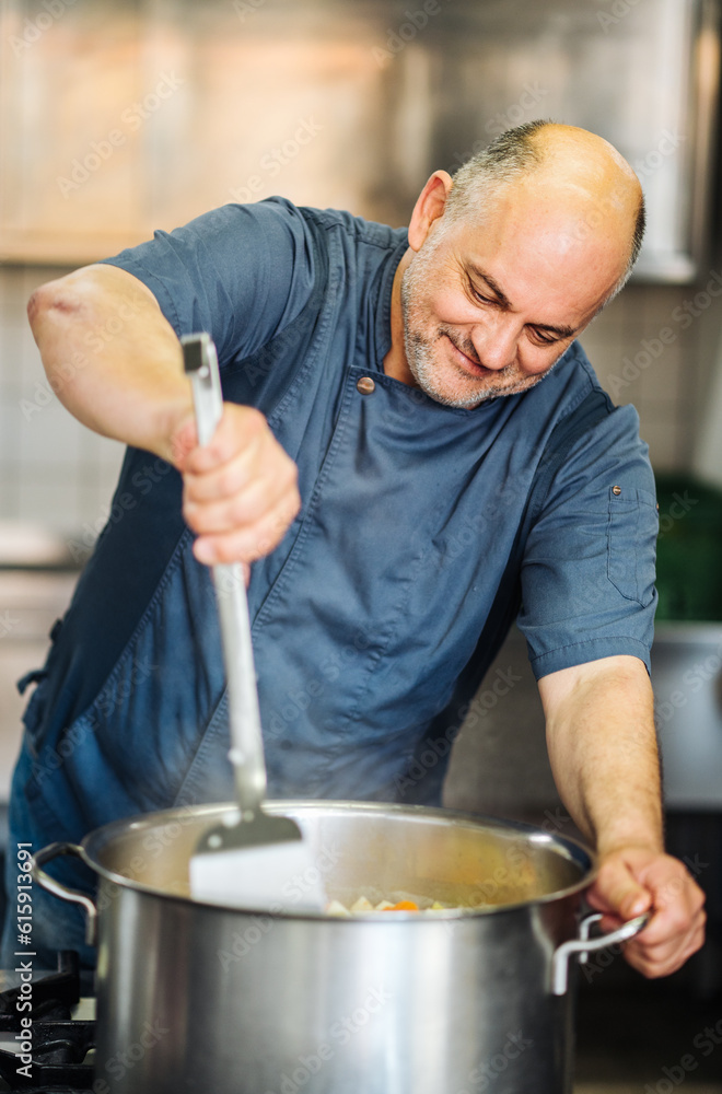 Koch in einer Großküche mit Freude bei der Arbeit. Hält eine große ...