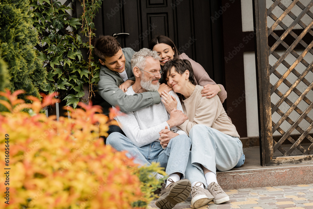 Smiling children hugging happy middle aged parents while sitting on ...
