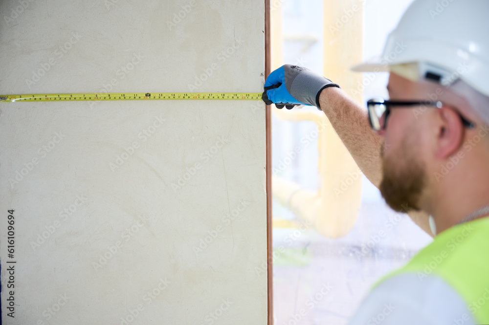 Construction worker measuring a wall in the new house with roller tape ...