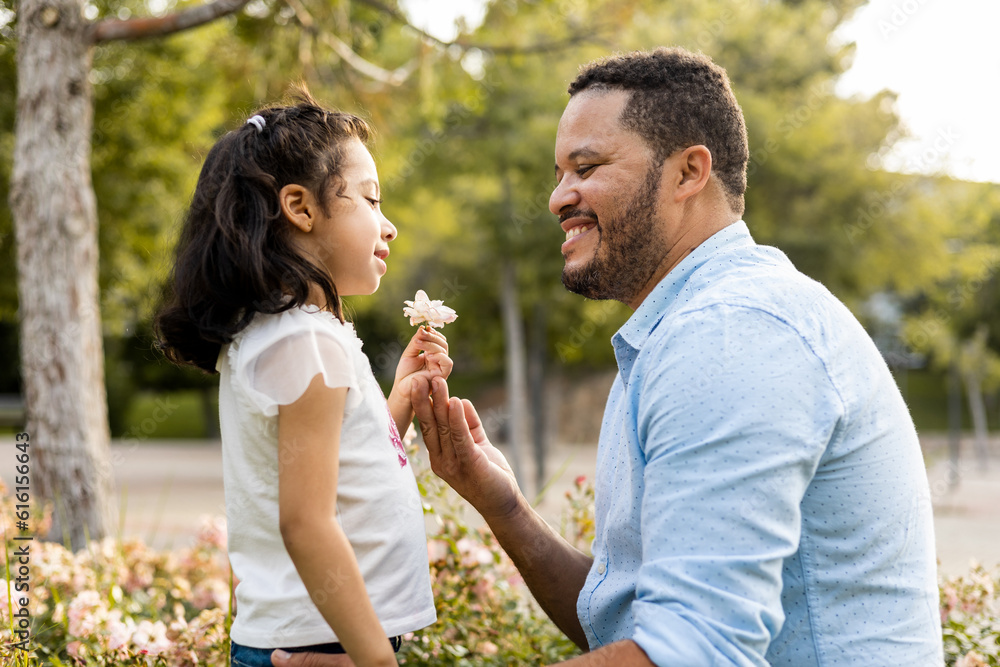 A dark-skinned father plays with his daughter in an outdoor park. The ...