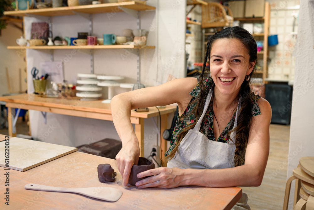 Smiling woman in studio working raw ceramic and clay to make pot ...