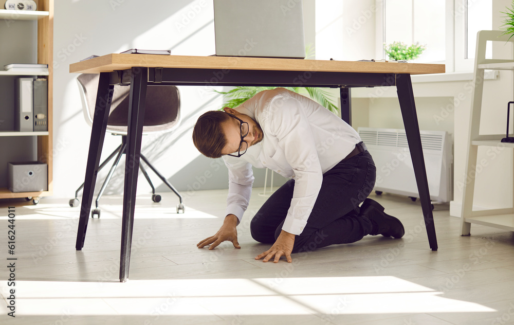 Man hides under table during earthquake. Man sitting on floor under ...