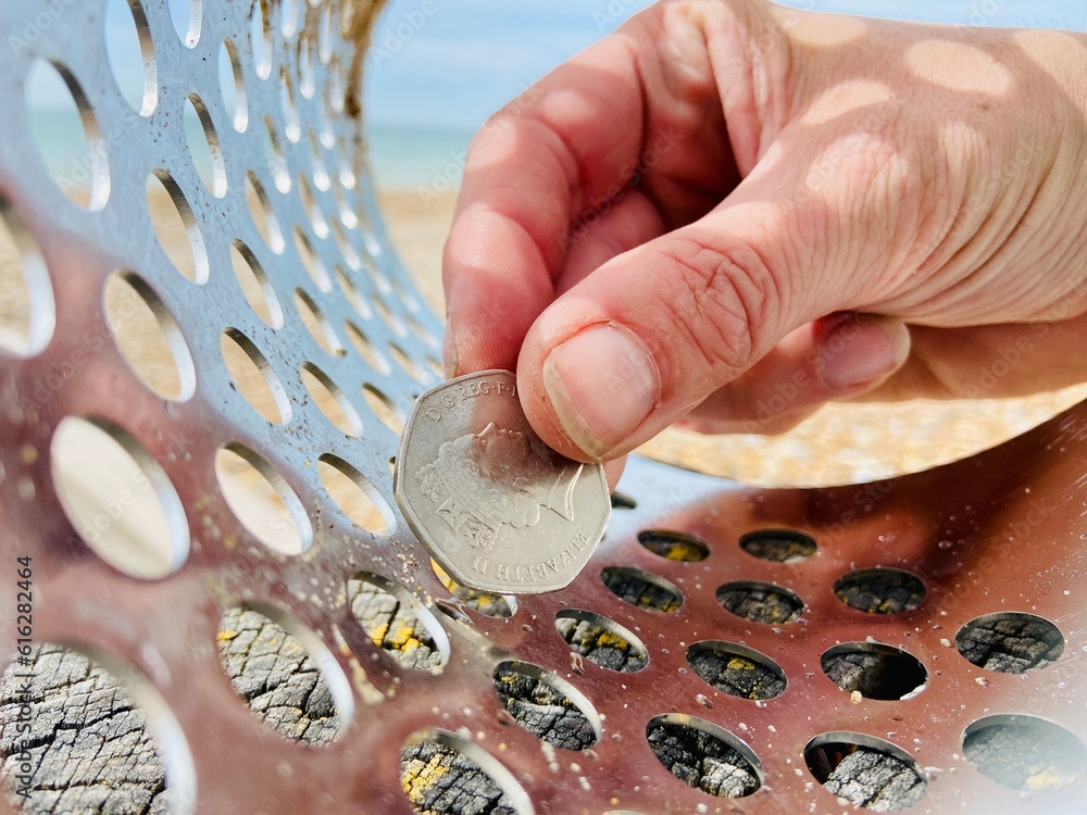 coin in beach sand scoop with metal detector coil on sand in background ...