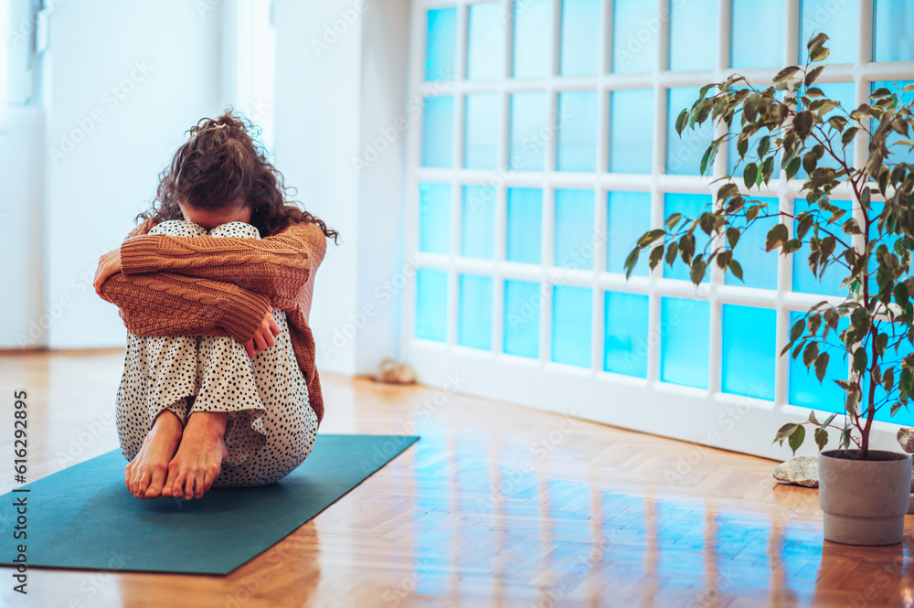 Curly girl bowing her head while sitting with her arms around her bent ...