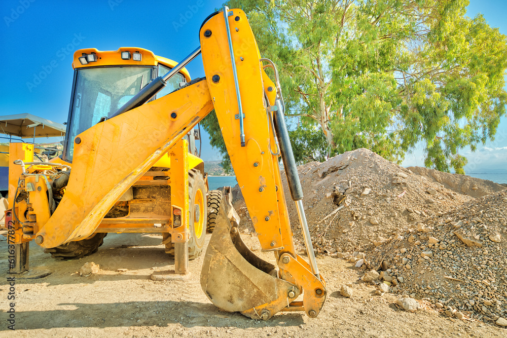 Side view of yellow excavator with long arm along coastal road. Work in ...