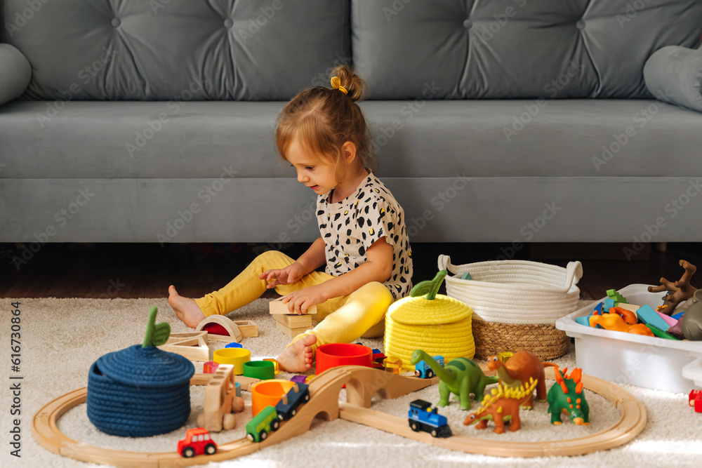 Kid girl builds a toy town and wooden railway. A little girl sitting on ...