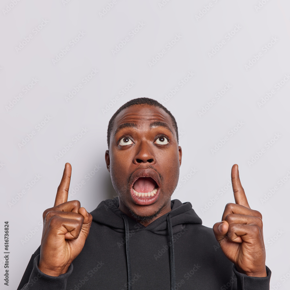 Stupefied African man dressed in casual attire points upwards with wide ...
