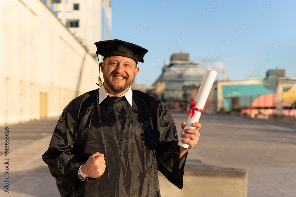 Man recent graduated, dressed in cap and gown, showing off his degree ...