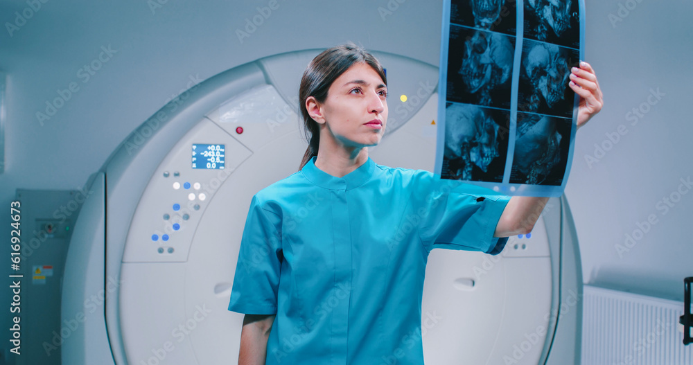 Young nurse in blue coat carefully examines MRI scan. Female medical ...